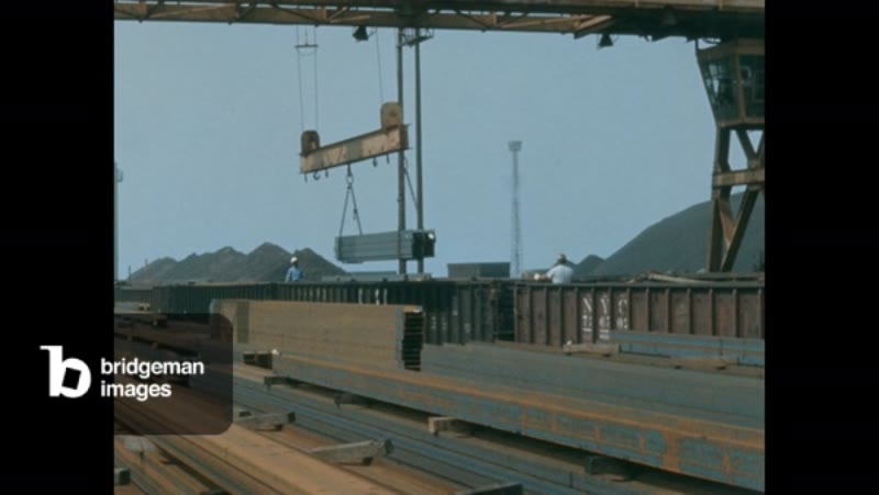 Image of 1960s: Men by train, crane moving metal bars.